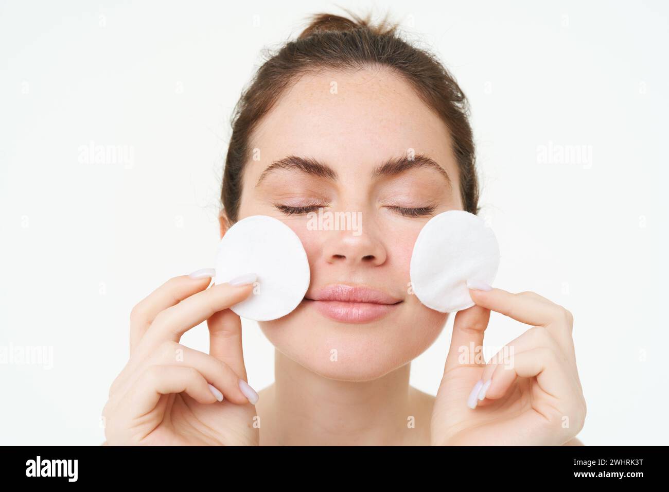 Image of young woman taking off her makeup with cotton pads, using facial cleanser, cleaning her ...