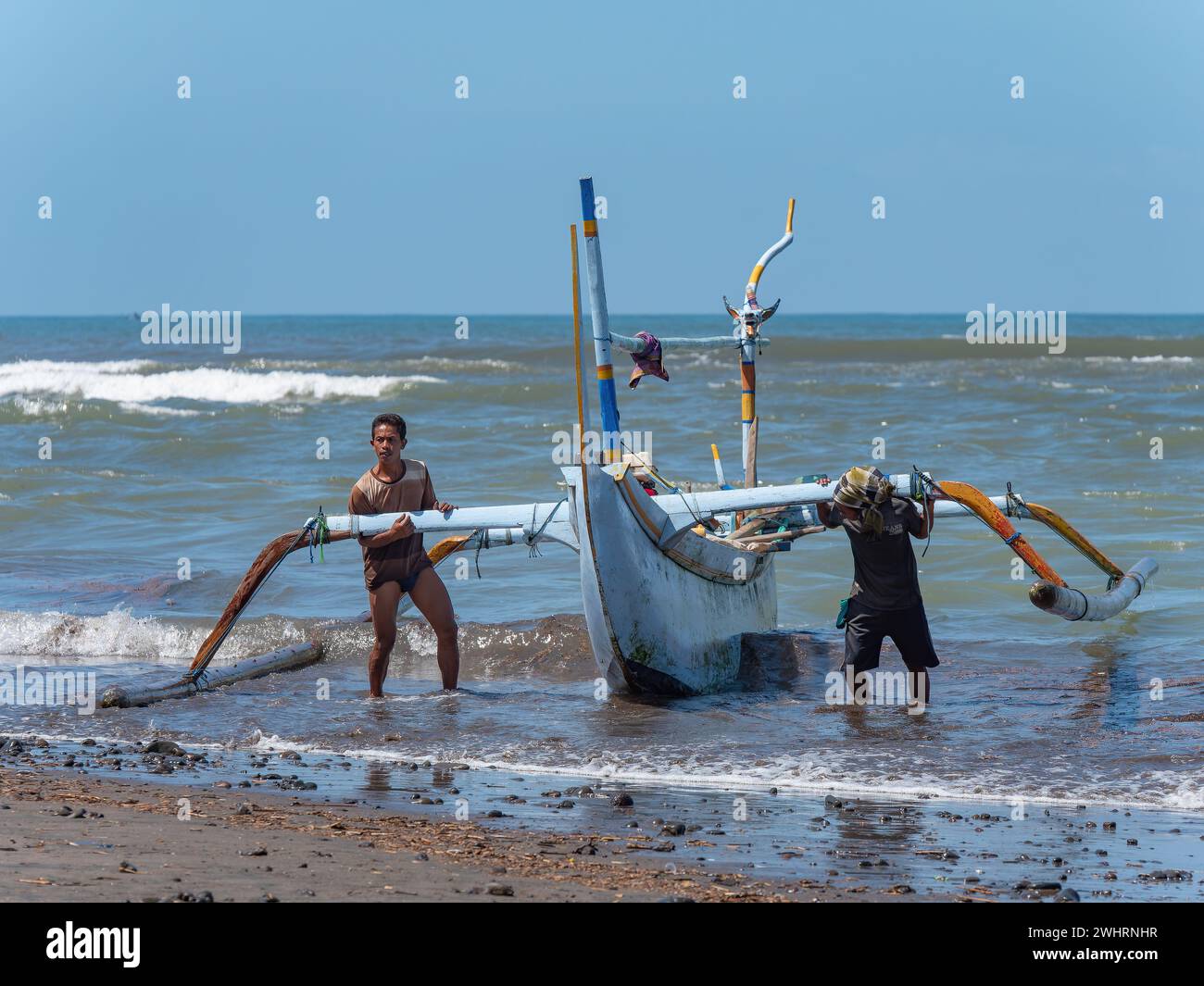 Traditional Indonesian fishing boat with outriggers arriving at a stony ...