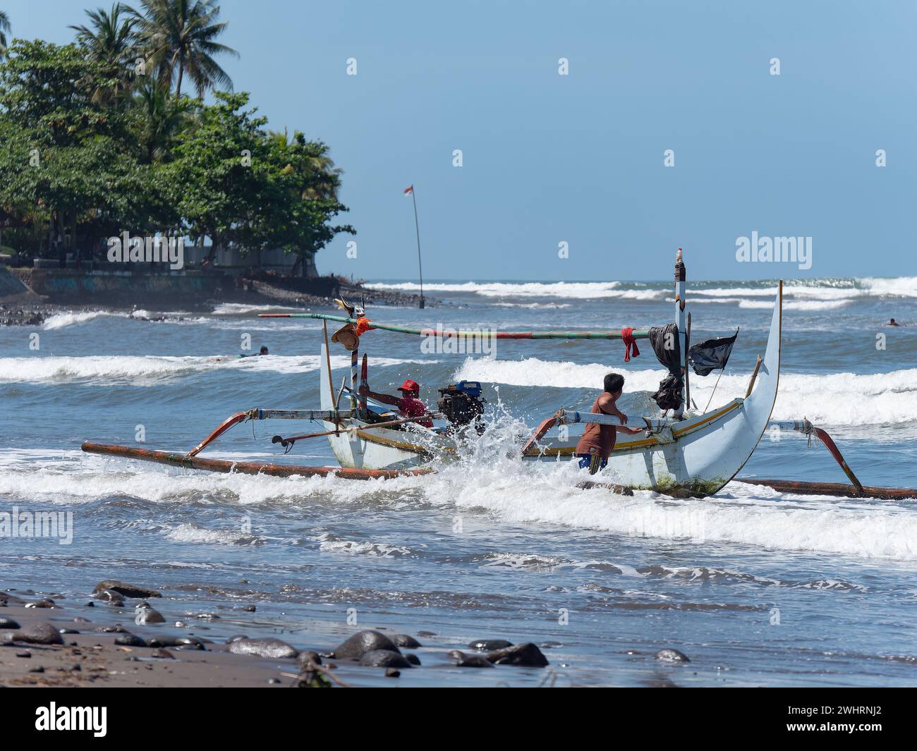 Traditional Indonesian fishing boat with outriggers arriving at a stony ...