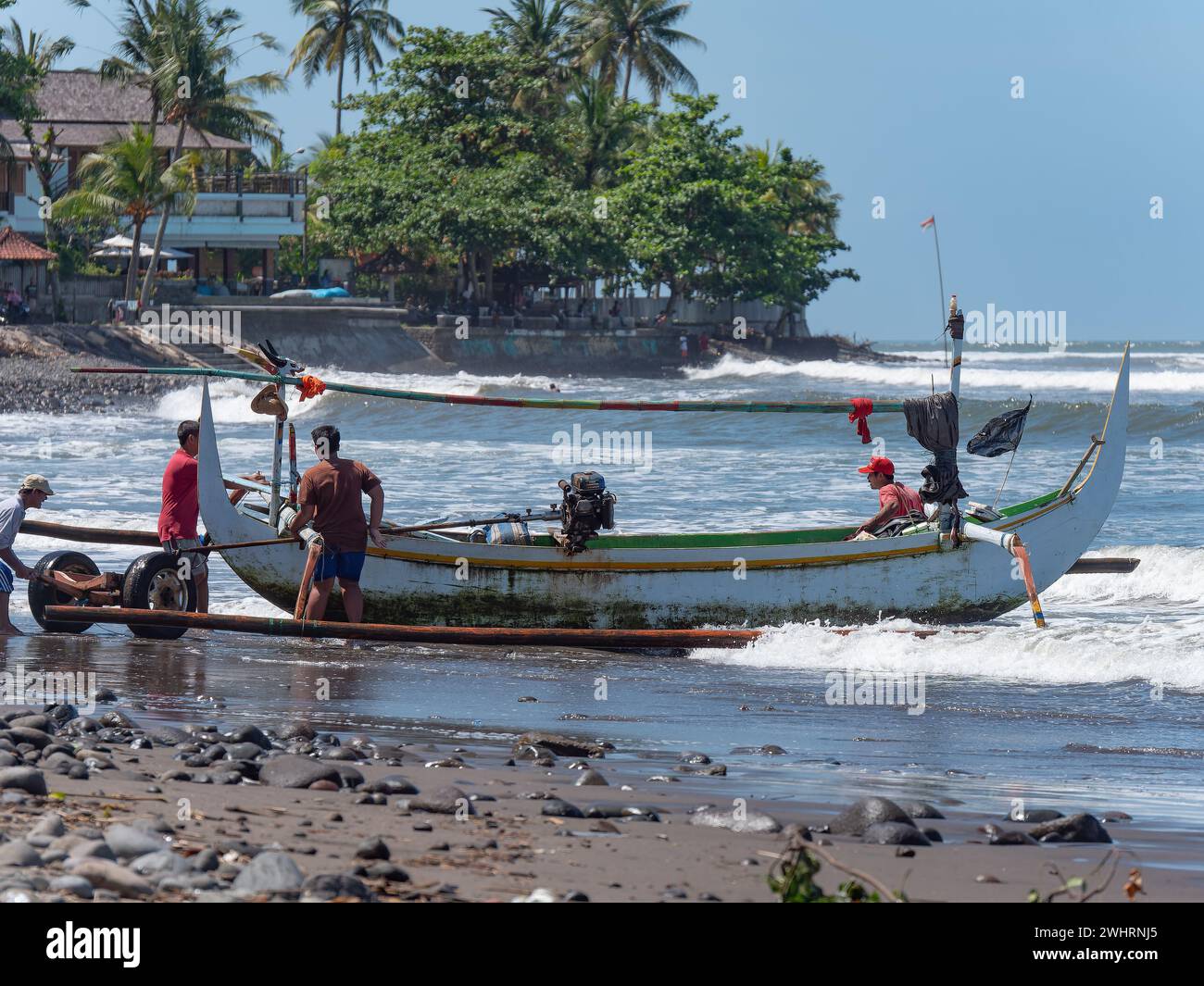 Traditional Indonesian fishing boat with outriggers being hauled onto a ...