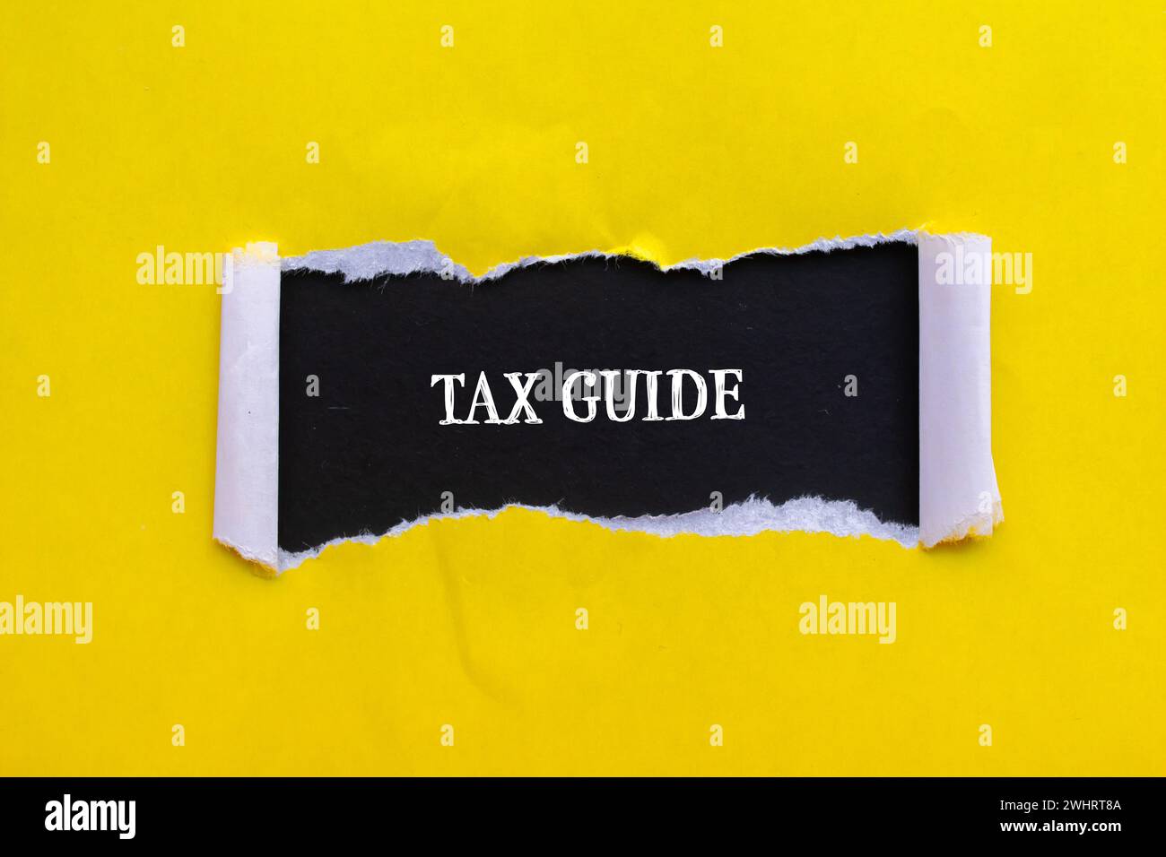 Tax guide words written on torn yellow paper with black background ...