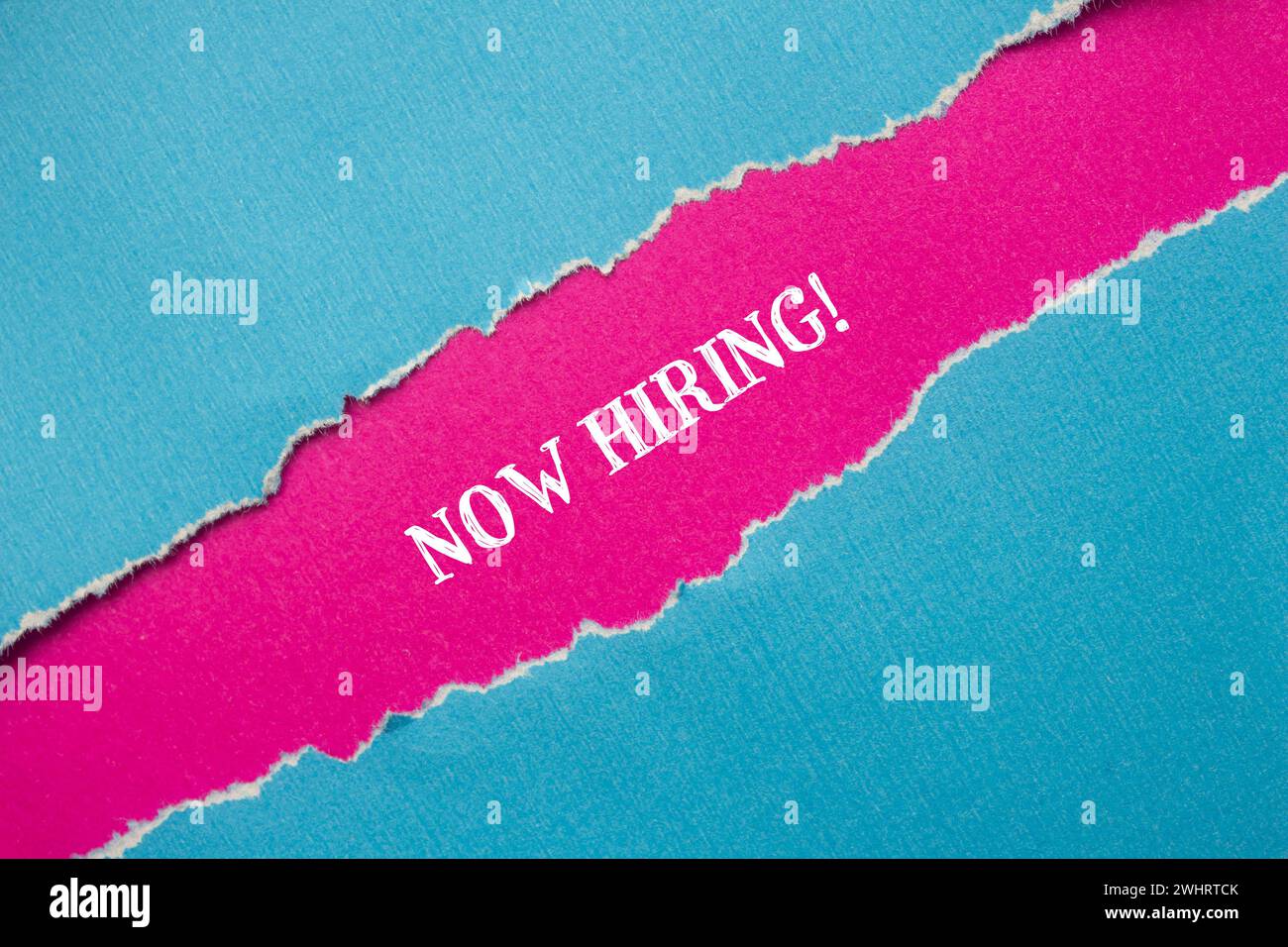 Now hiring words written on blue torn paper with pink background ...