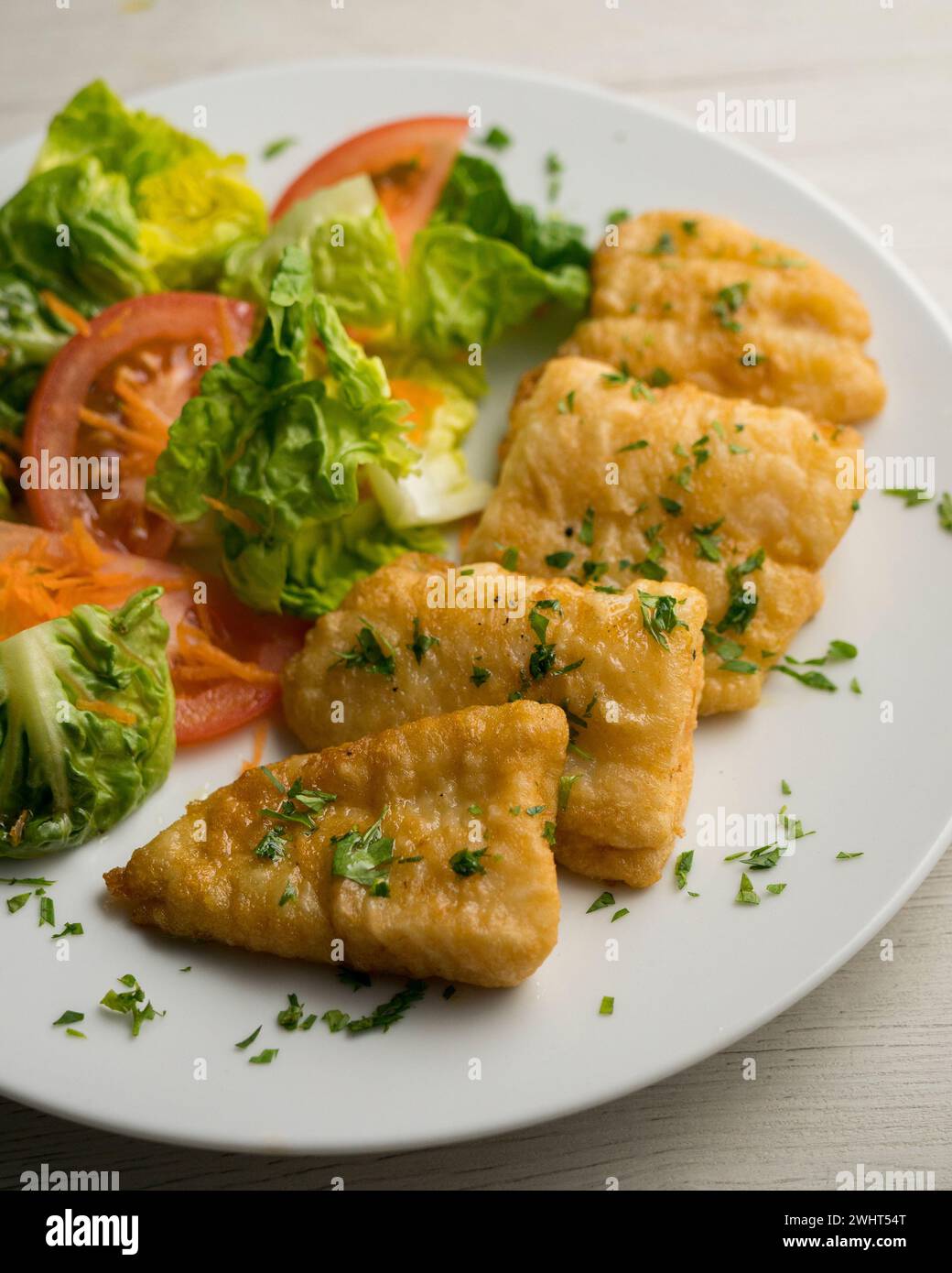 Battered white fish served with a tomato salad Stock Photo - Alamy