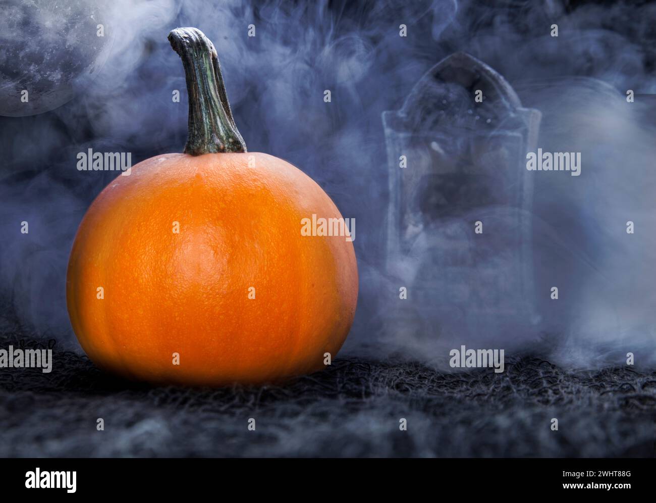 Smoke emerges from a vibrant orange pumpkin resting on a sleek black ...