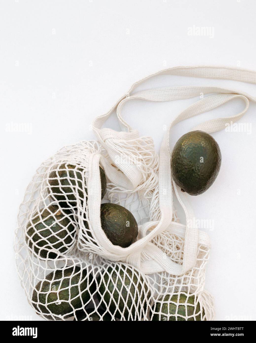 Avocados in a white net bag on a clean background, emphasizing ...