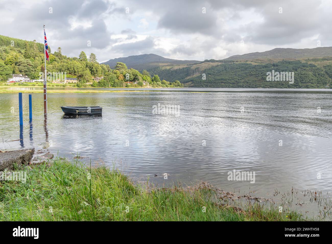 Union Jack flag on a pole with a boat tied up at high tide in sea Loch ...