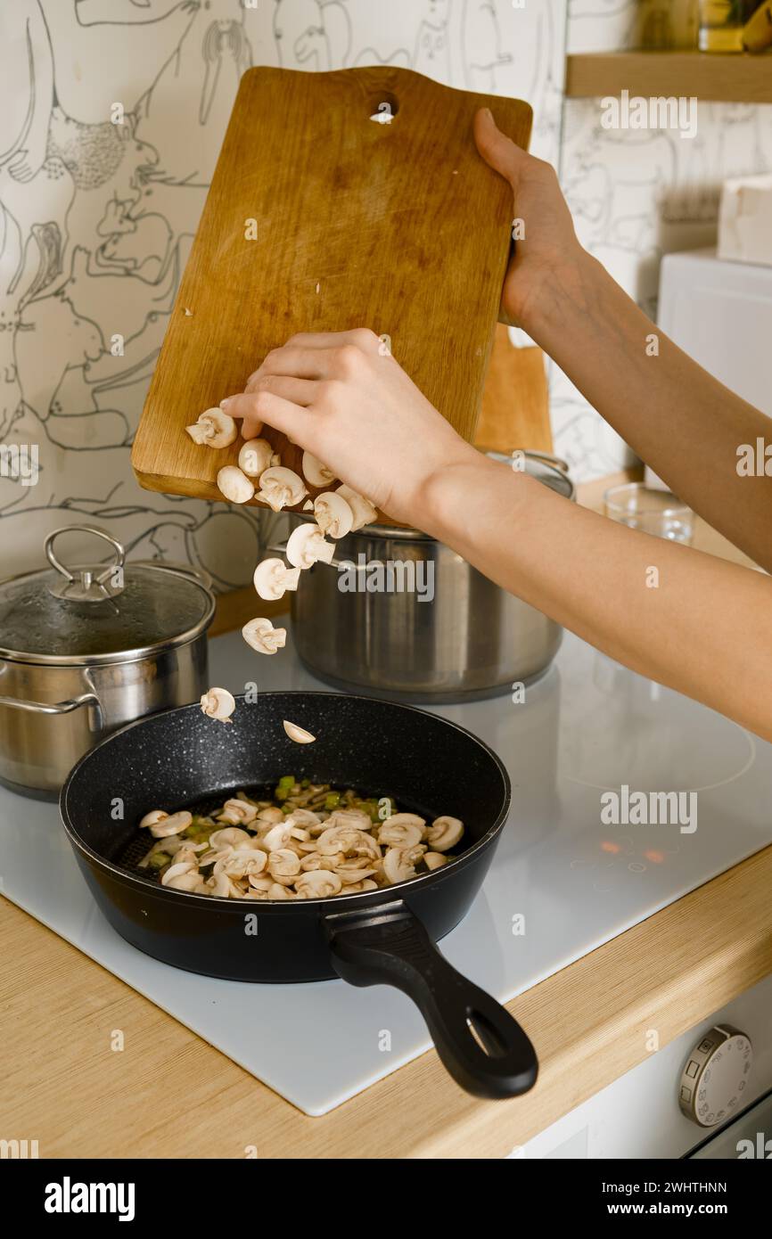 Woman adding chopped champignon to a frying pan in the kitchen Stock ...