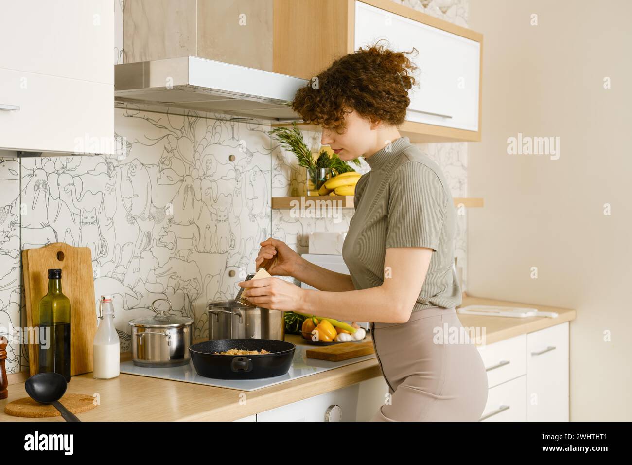 Woman grating parmesan cheese into a frying pan with cooked pappardelle ...