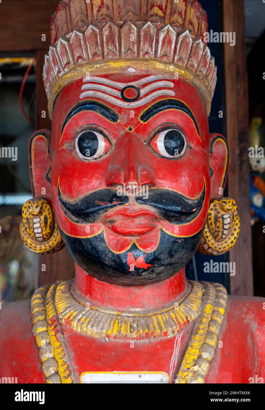 A close-up of a traditional red-faced statue of a man with a mustache ...