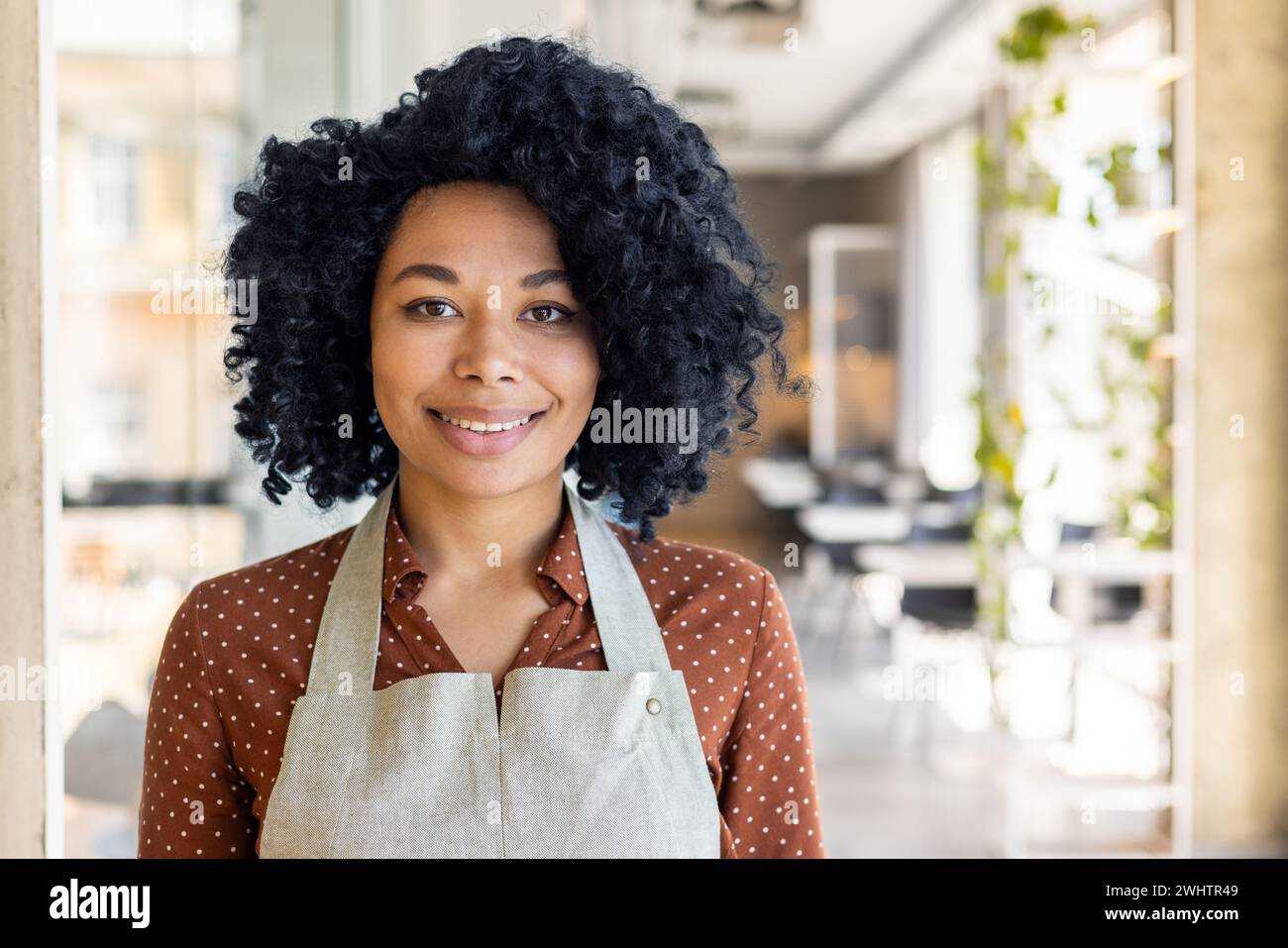 Portrait of brunette diverse smiling lady wearing apron over blouse ...