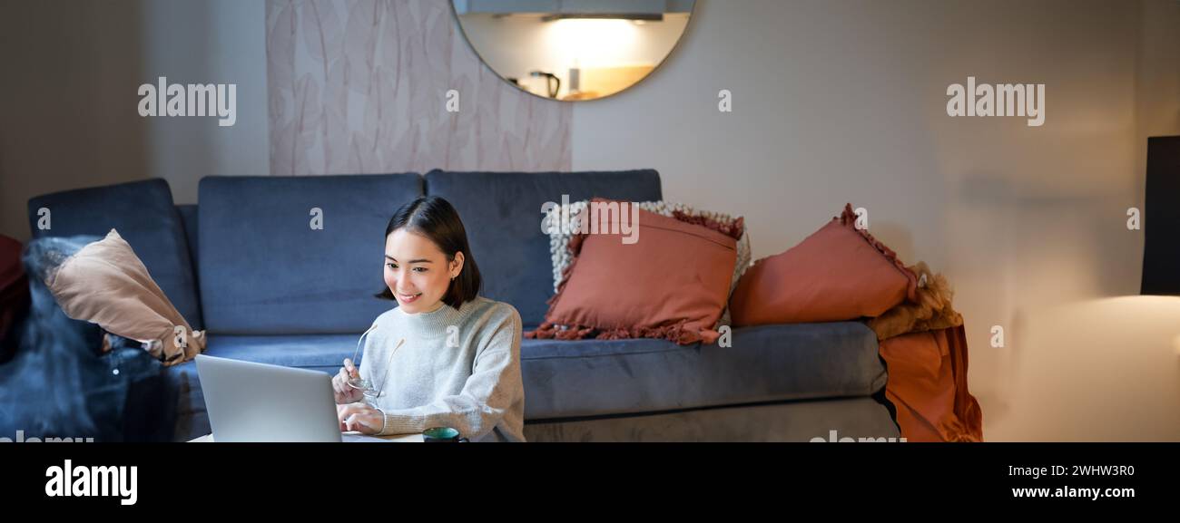 Vertical shot of asian girl sits on floor at home, working on laptop ...