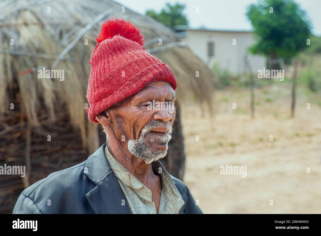 african village ,old man standing in the yard in front of the mud house ...