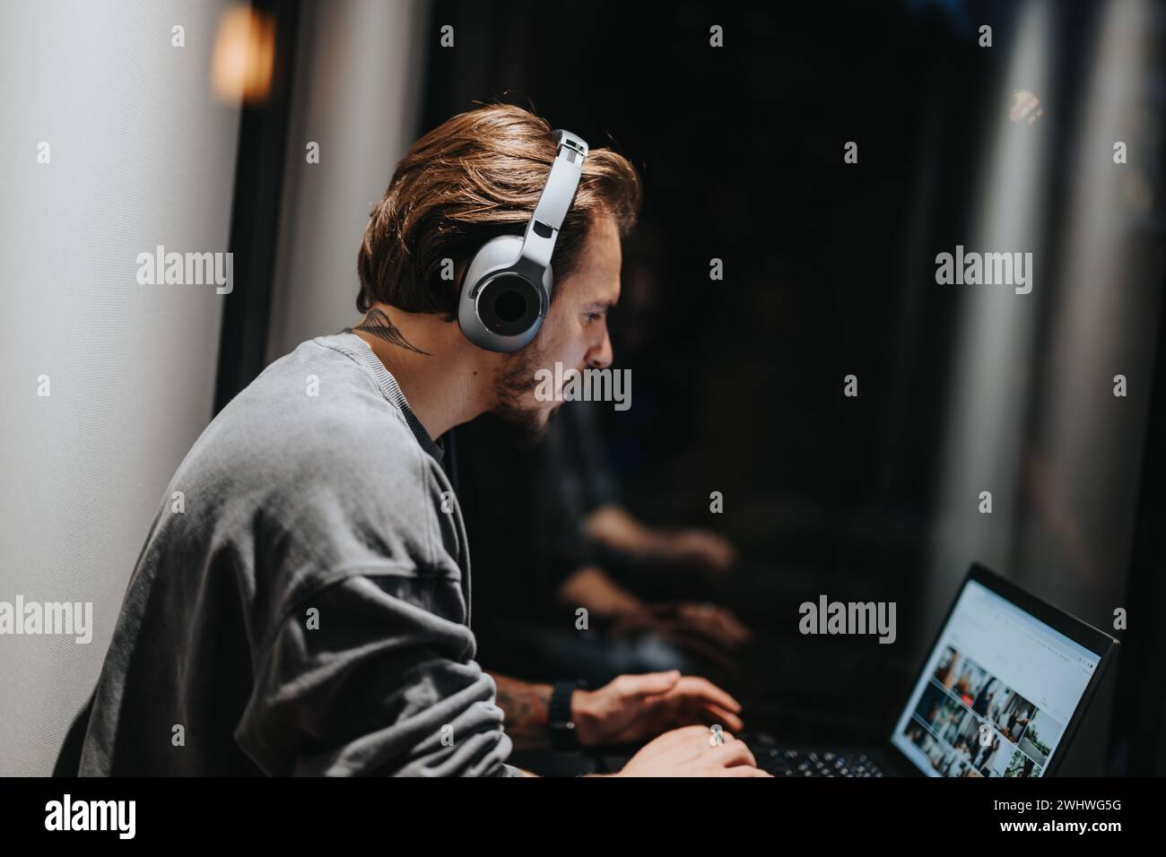 Focused male professional working intensely on laptop with headphones ...