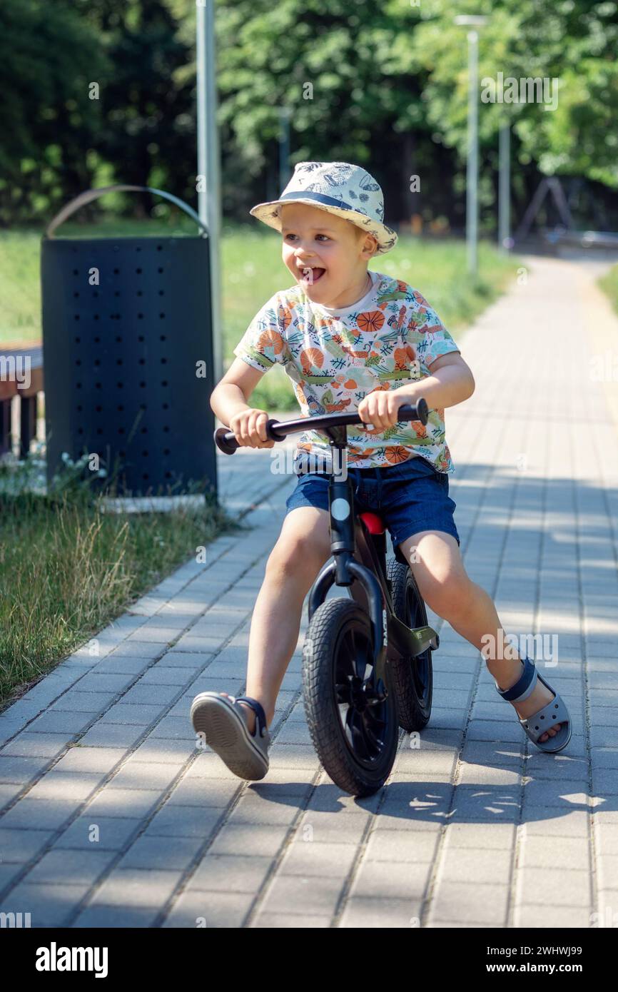 A very cheerful laughing boy is running fast on his balance bike in the summer park Stock Photo ...