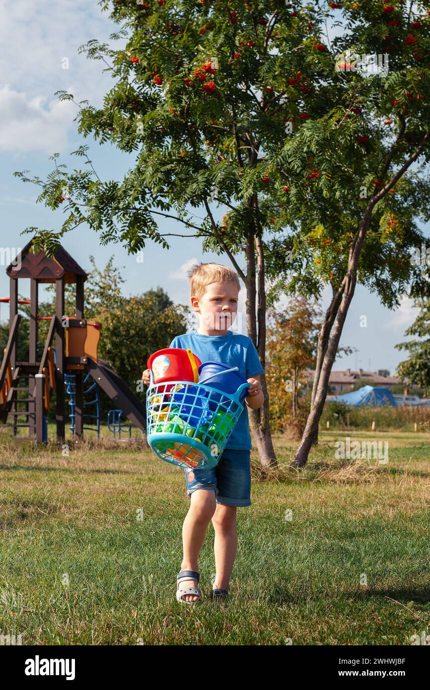 A sad little boy with his bag full of colorful toys in the outdoor ...