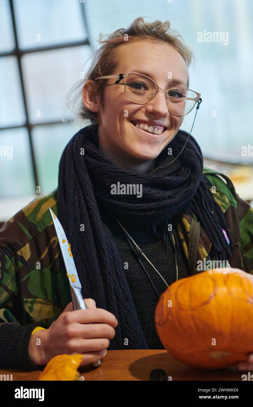 A modern blonde woman in military uniform is carving spooky pumpkins ...