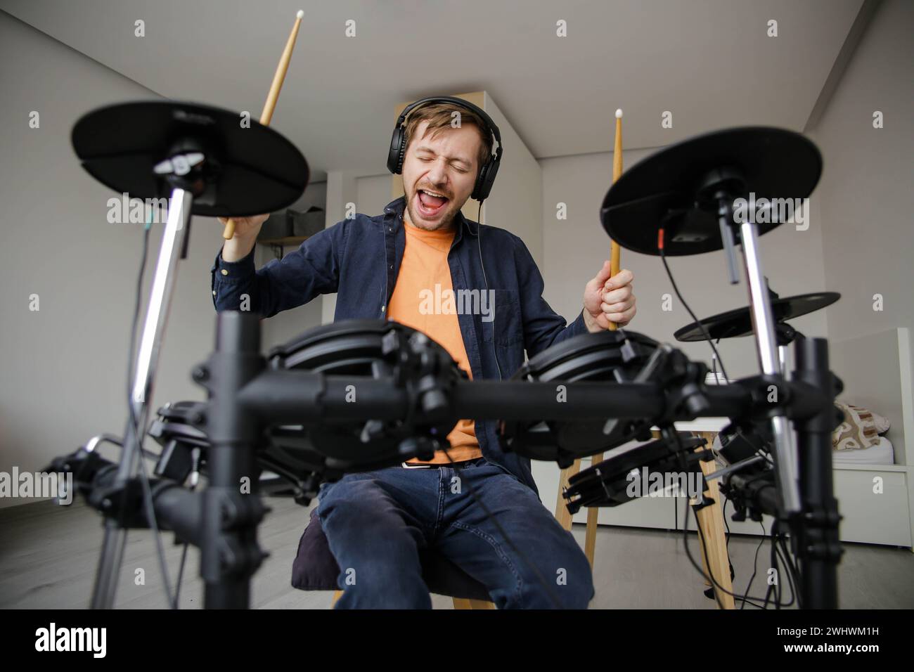 Excited young man with headphones hitting electric drum set during ...