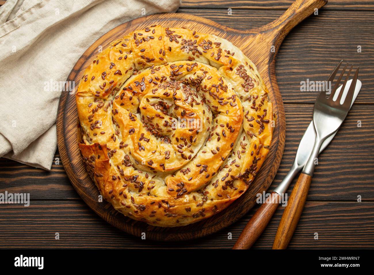 Burek made of phyllo dough with filling on cutting board, dark brown ...