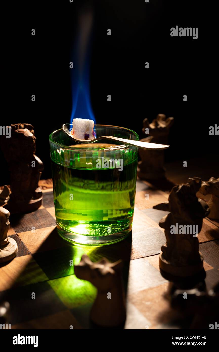 Preparing green absinthe with sugar and fire on a chess board Stock ...