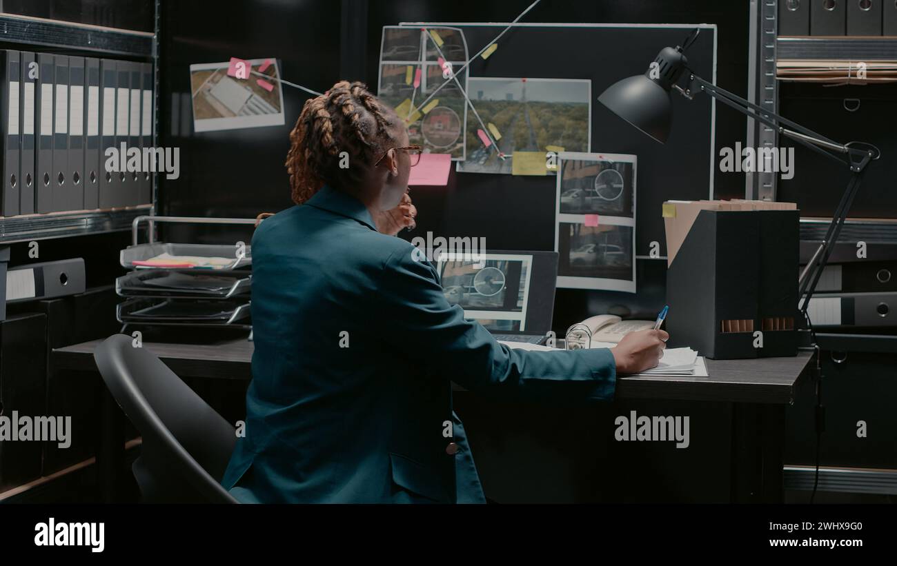 Police agent taking notes on case files in incident room, trying to ...