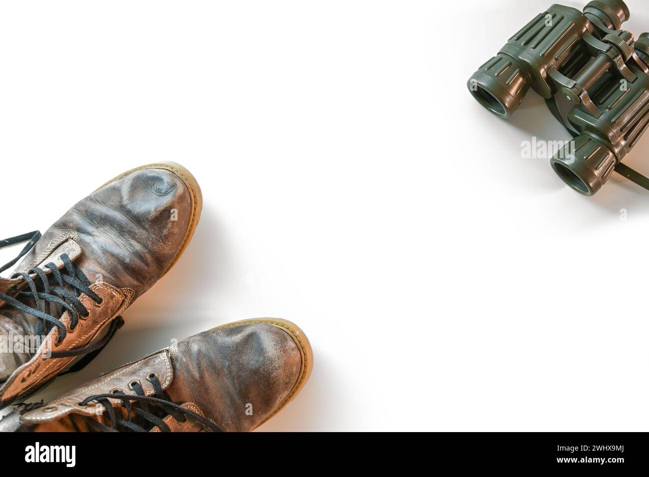 Old trekking boots and binoculars at the corners of a white background ...