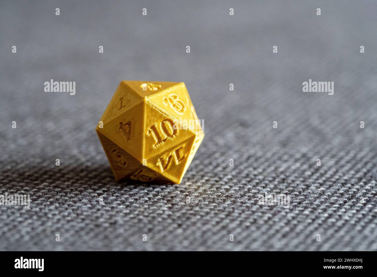Golden 3D printed d20 RPG game dice on a bed object macro detail ...