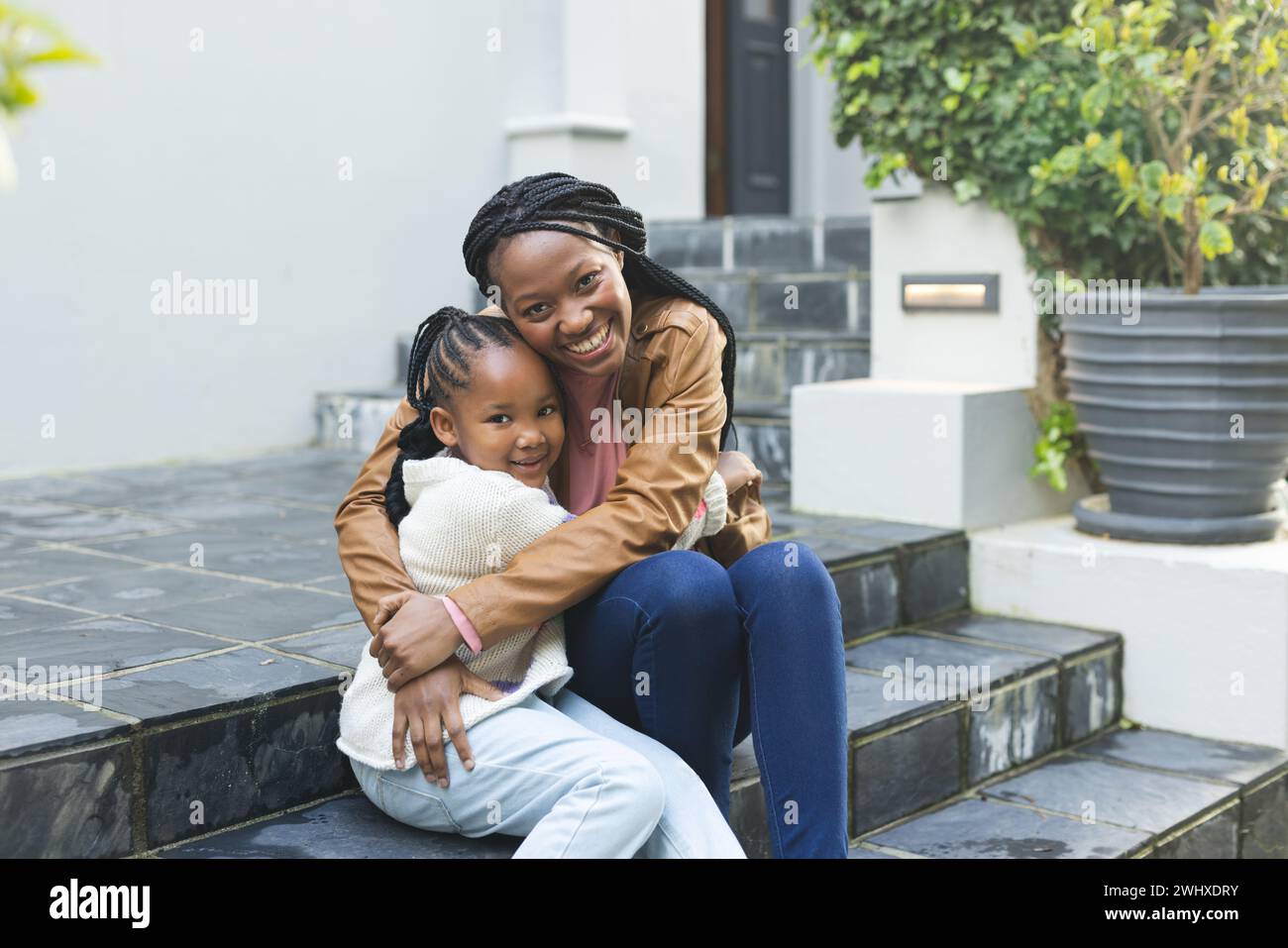 Happy african american mother and daughter embracing on steps in front of house Stock Photo - Alamy