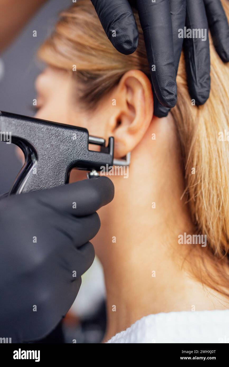 Close up of face of young blonde woman doing ear piercing procedure ...