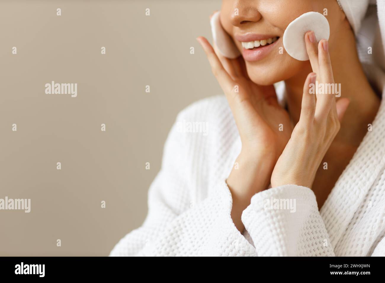 Pretty woman in robe and towel on her head wipes the skin of her face ...