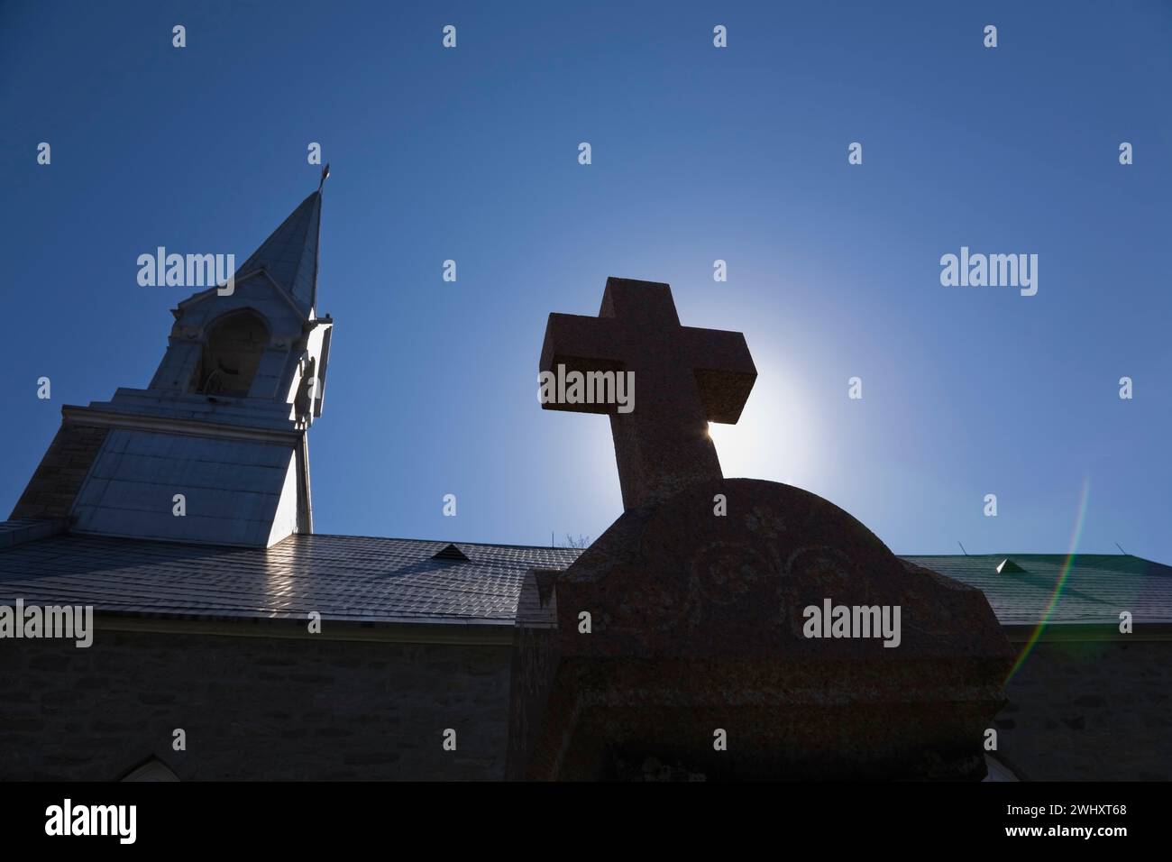Silhouetted granite cross atop headstone in cemetery and partial view ...