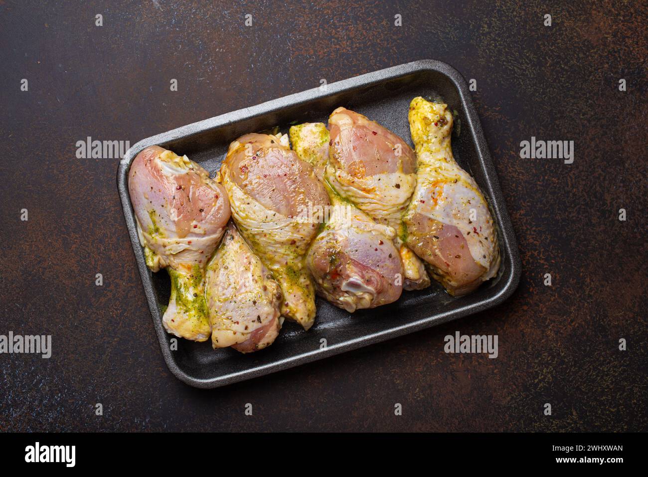 Raw uncooked chicken legs in green marinade with seasonings in black ...