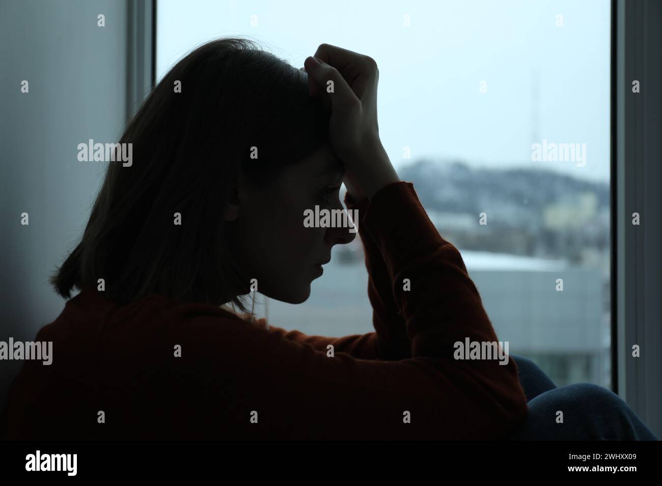 Sad young woman near window at home Stock Photo - Alamy