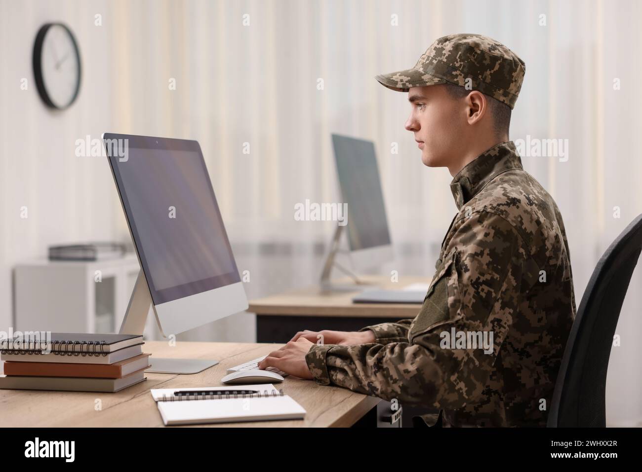 Military service. Young soldier working with computer at wooden table ...