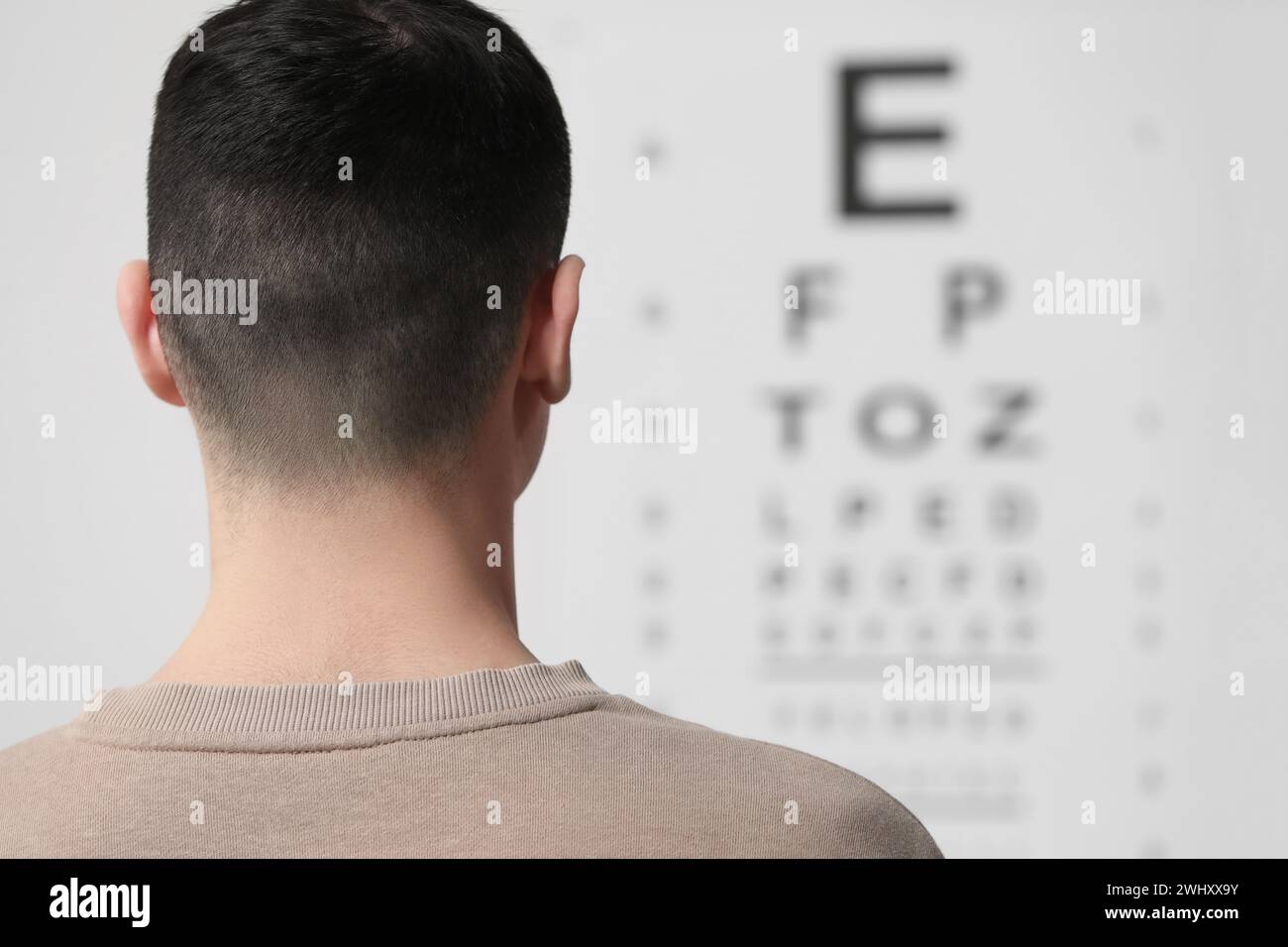 Eyesight examination. Young man looking at vision test chart indoors ...