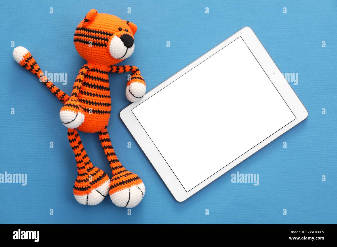 Modern tablet and toy tiger on blue background, flat lay. Space for ...