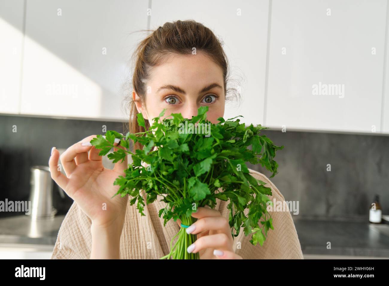Portrait of beautiful woman cooking, holding fresh parsley, adding ...