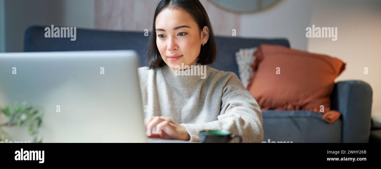 Self employed young korean woman working on remote, typing on laptop ...