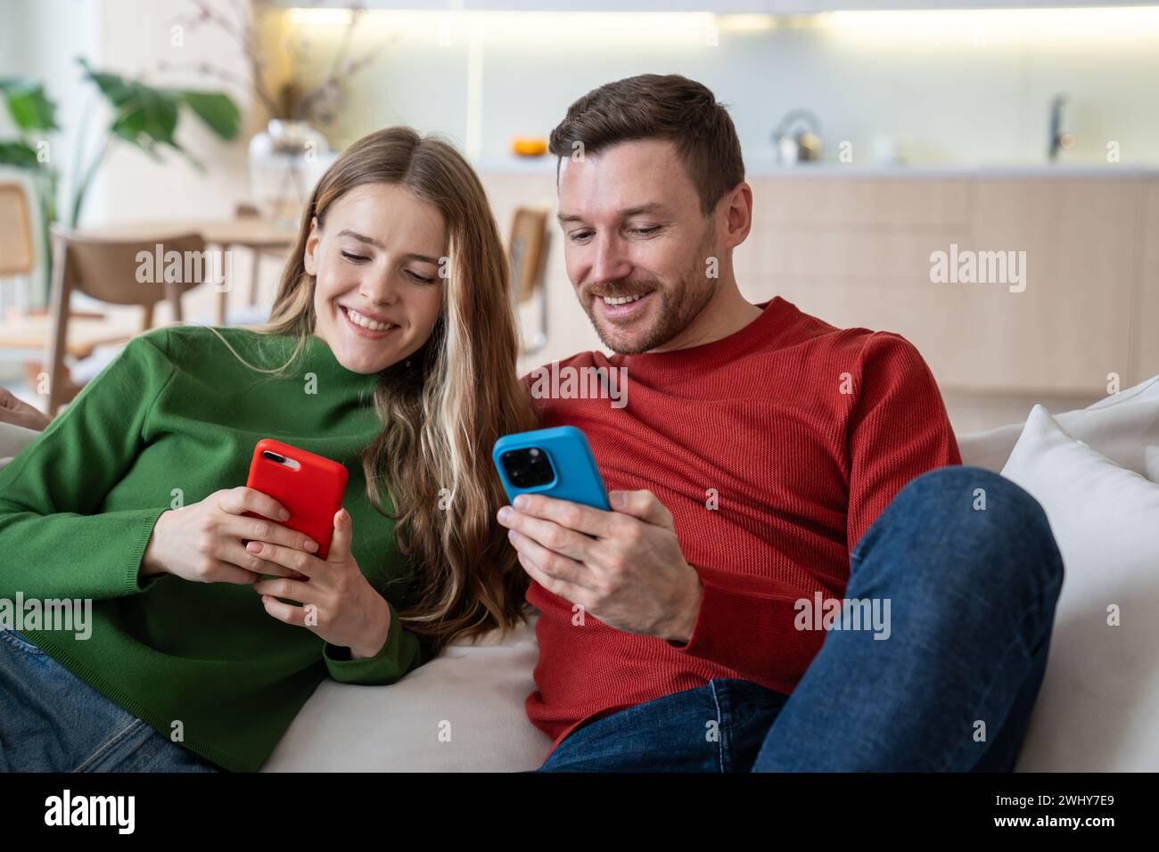 Smiling couple sitting with mobile phones, having group video call with ...