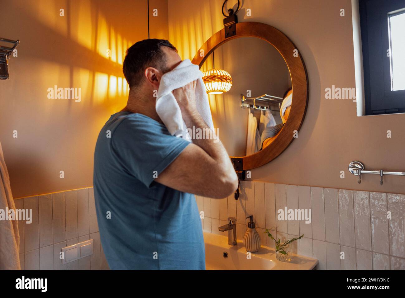 Young attractive man looks out the window and wipes his hands with ...