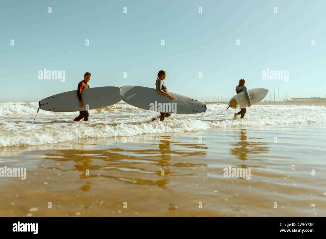 Group of happy surfers in wetsuit with his surfboards entering out of ...