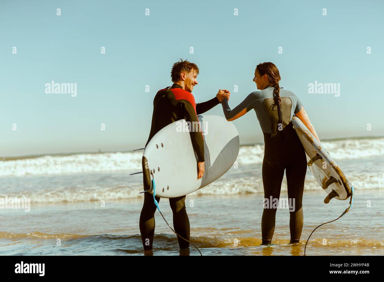 Two surfers greet each other by shaking hands before surfing on waves ...