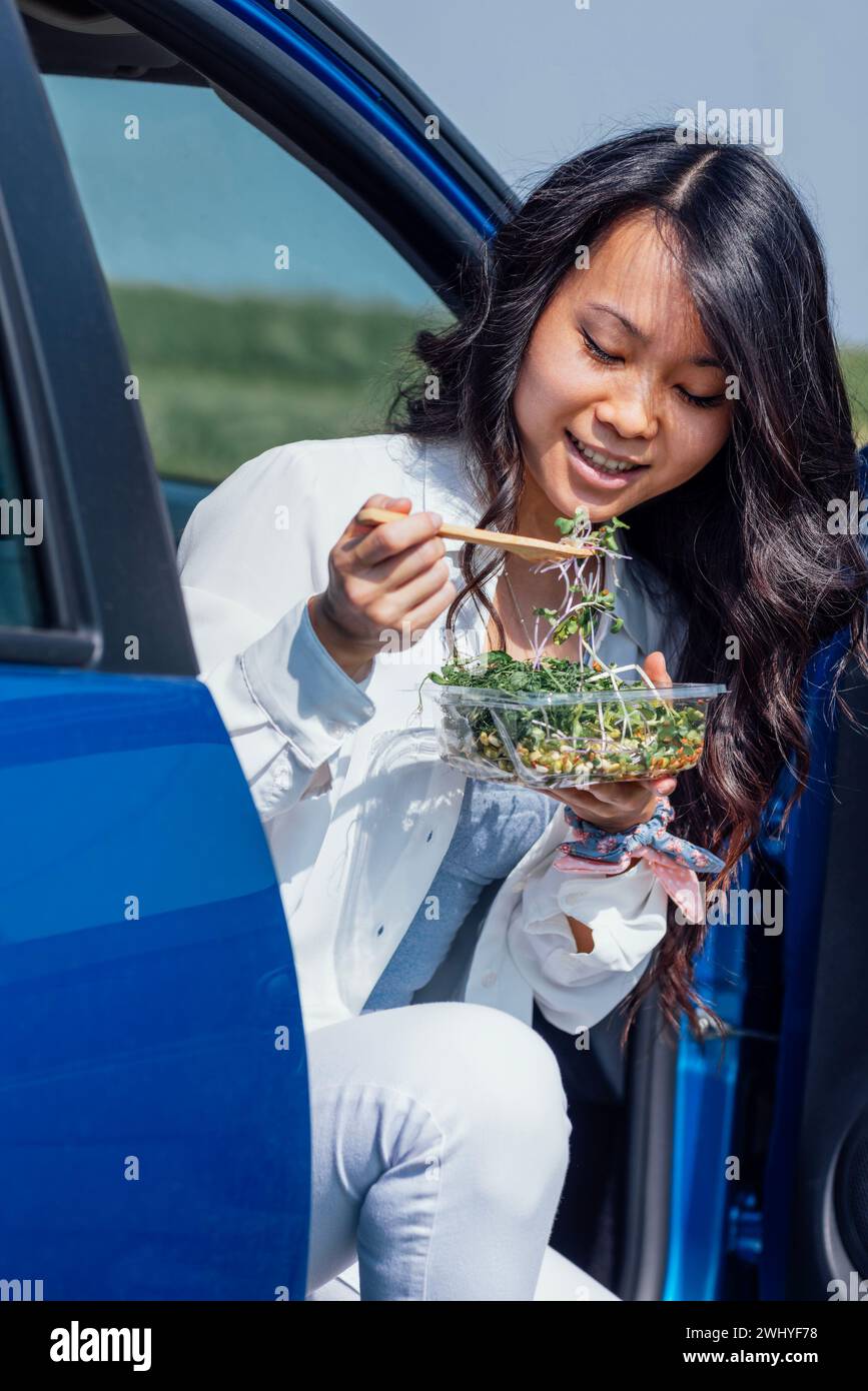 A young beautiful Korean woman in white clothes is eating a fresh salad ...
