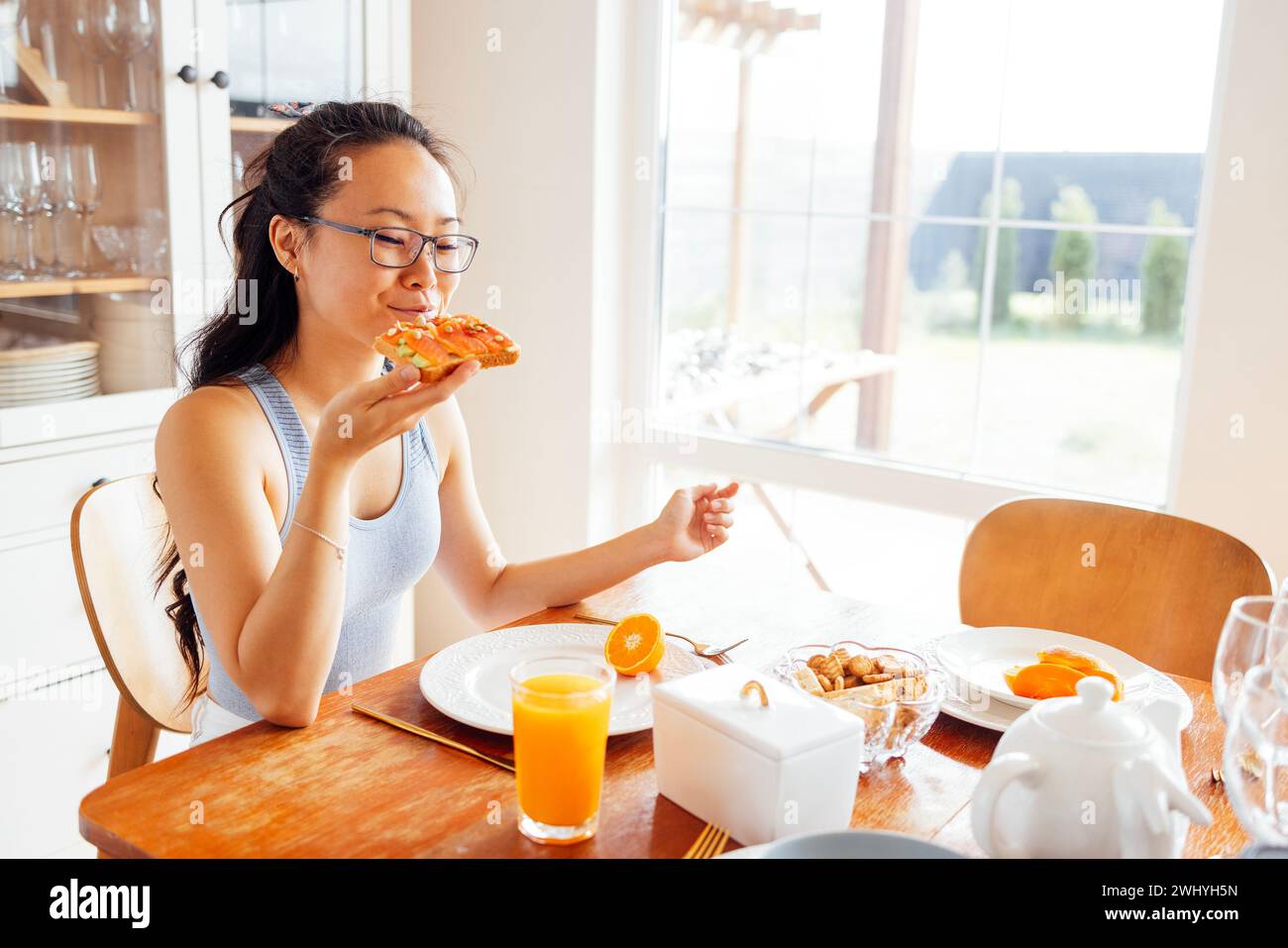 Young attractive Asian woman in glasses and casual clothes is sitting ...