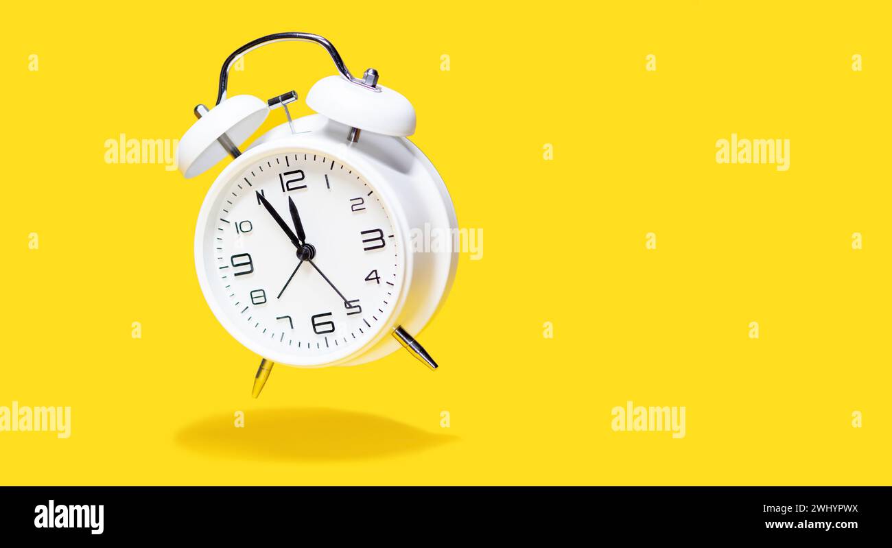 White bell alarm clock hovering over yellow background. 5 to 12 clock ...