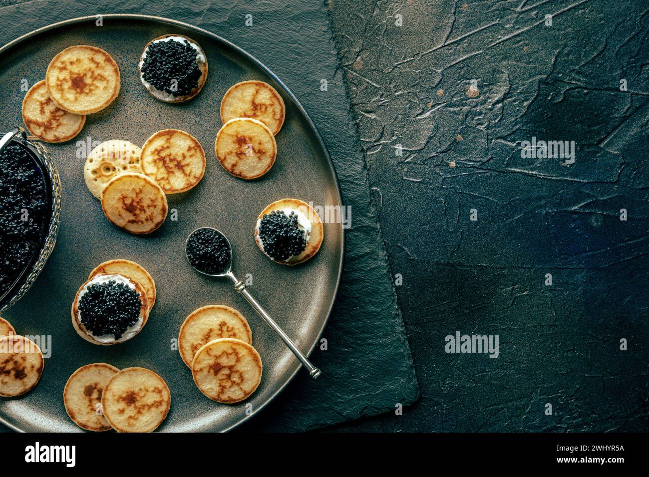 Blinis with black caviar and cream cheese, overhead flat lay shot on ...