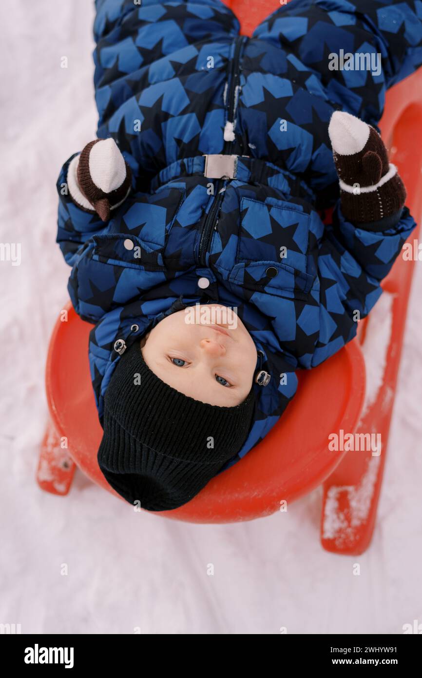 Little boy in a jacket and hat lies on a sleigh. Top view Stock Photo ...