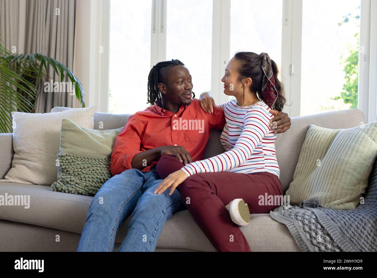 Happy diverse couple sitting on couch relaxing and talking in sunny ...