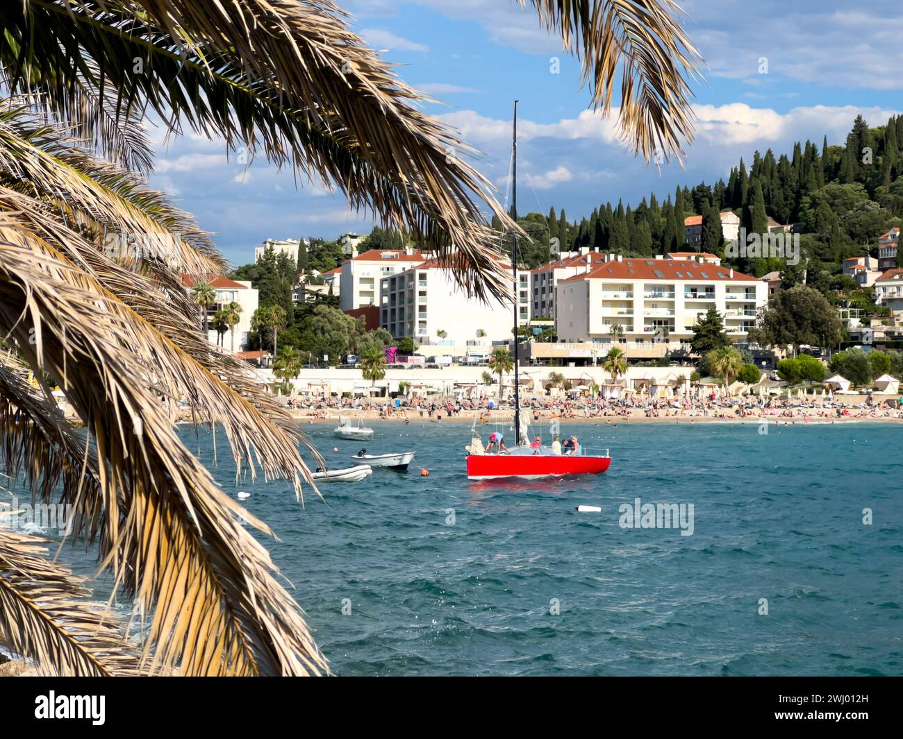 Red sailing yacht sails on the sea against the backdrop of a crowded ...