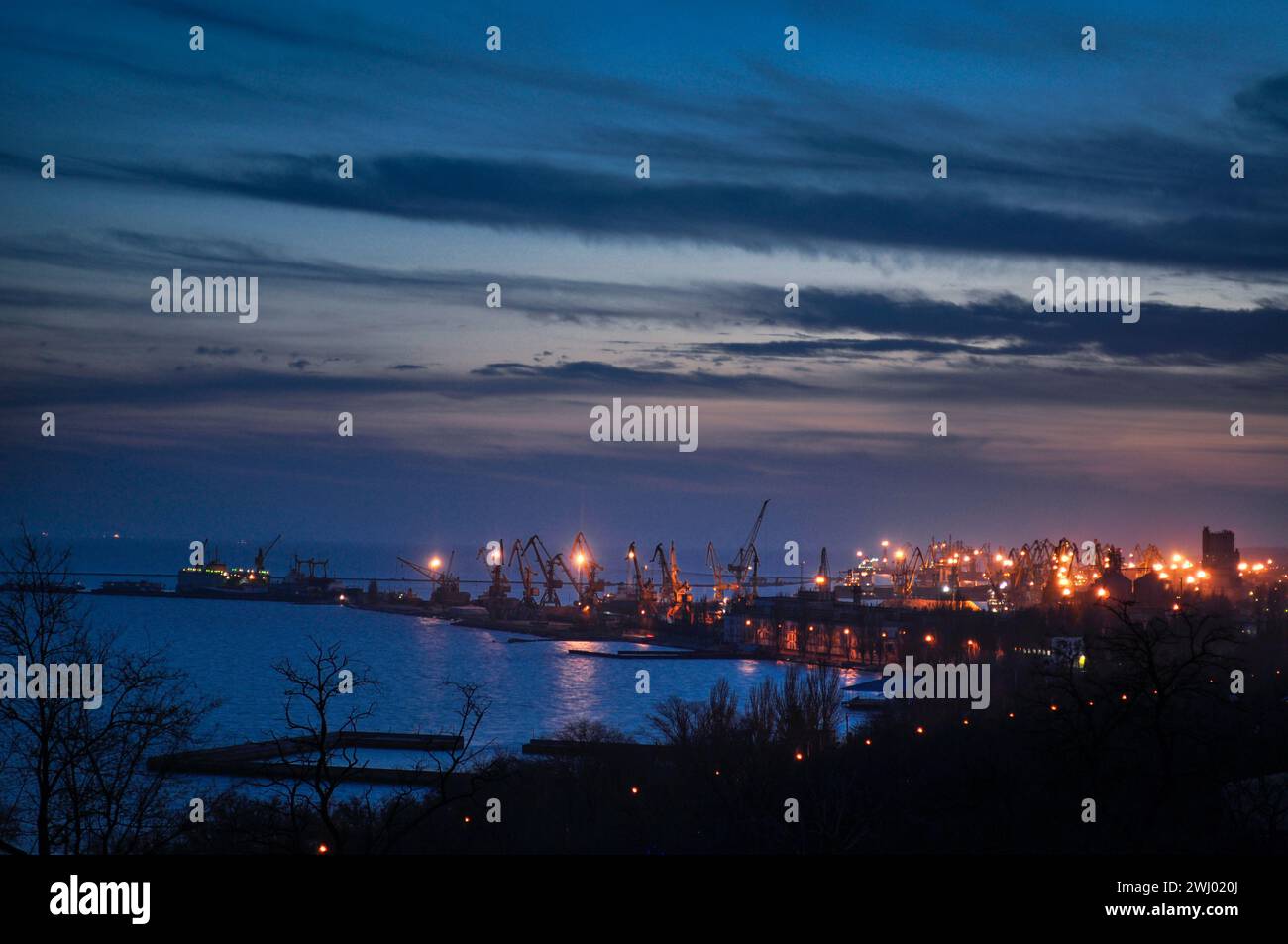 Twilight over industrial harbor with cargo cranes, lit buildings ...