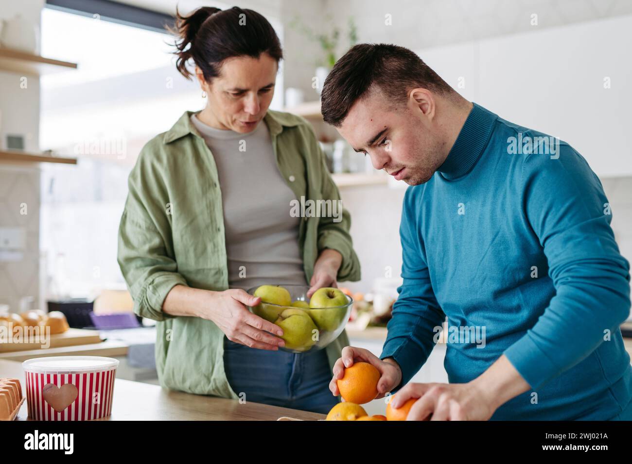 Young man with Down syndrome preparing breakfast with his mother at ...